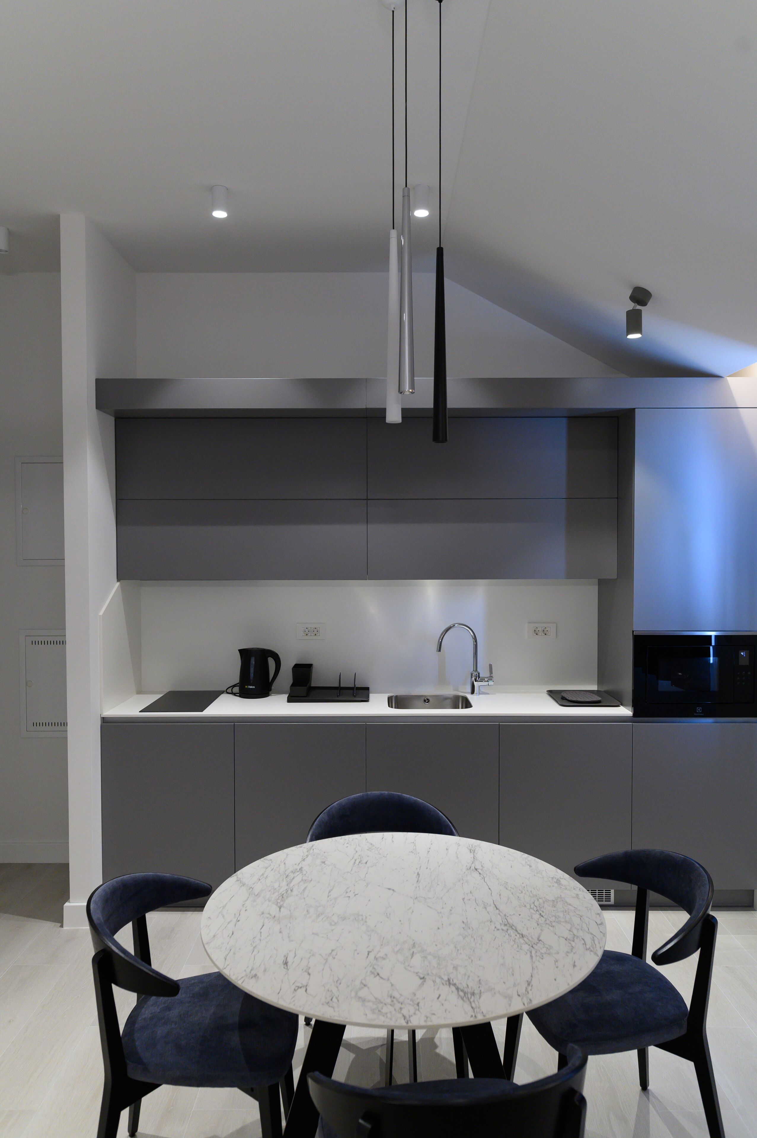 Cozinha moderna com bancada de mármore, eletrodomésticos embutidos e área de jantar com mesa e cadeiras redondas.