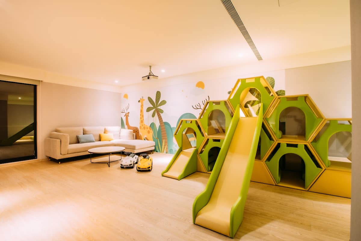 Uma sala de estar moderna com um sofá bege, uma mesa de centro e uma área de recreação com estruturas hexagonais verdes e amarelas.