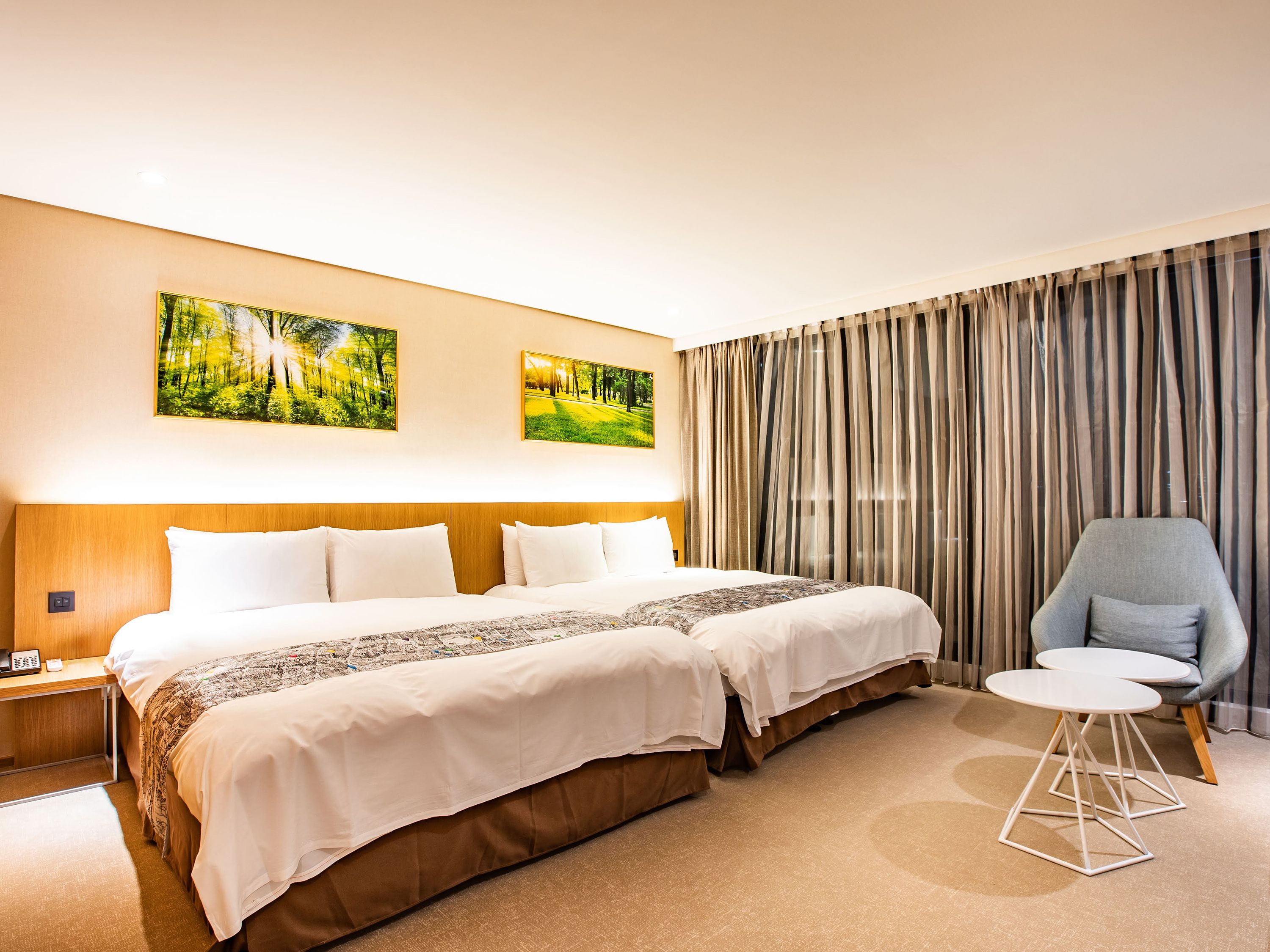 Quarto de hotel com uma cama grande, duas mesas de cabeceira, uma cadeira e vista para uma floresta através das cortinas.