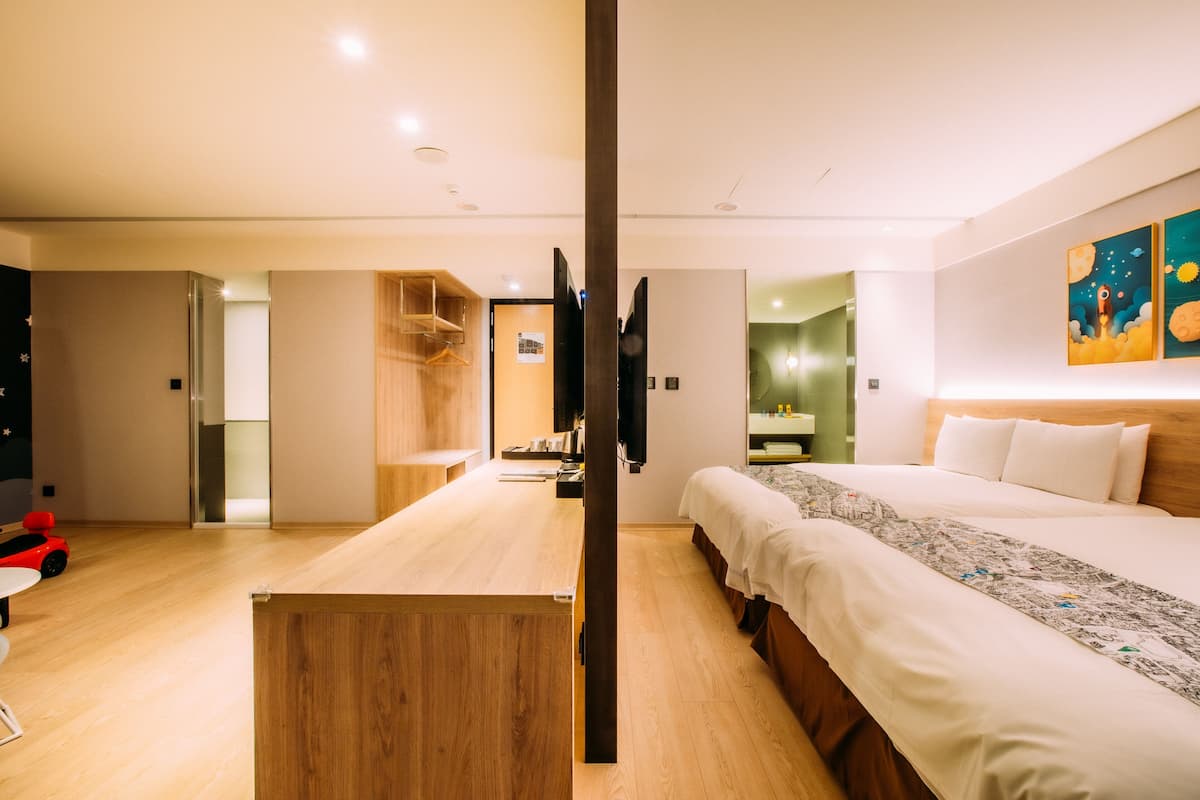Quarto de hotel moderno com piso de madeira, uma cama grande com roupa de cama branca, uma escrivaninha de madeira e uma televisão montada na parede.
