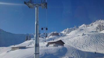 Um teleférico com cabines, um esquirolá e uma encosta de montanha coberta de neve com uma hospedaria e área coberta.