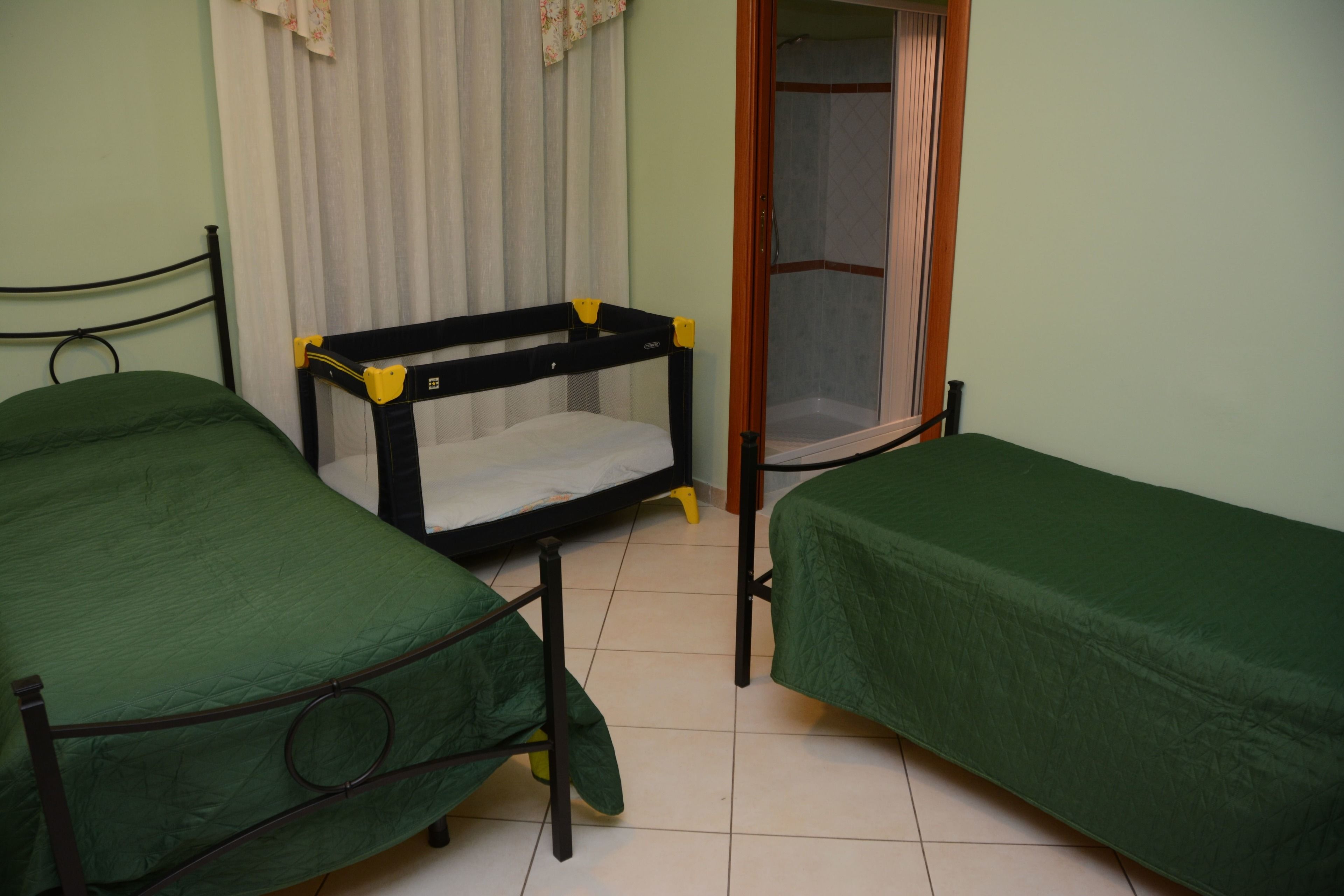Quarto com duas camas de solteiro, uma janela com cortinas e uma porta que dá para um banheiro.