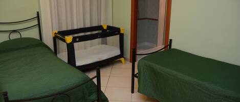 Quarto com duas camas de solteiro, uma janela com cortinas e uma porta que dá para um banheiro.