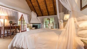Quarto espaçoso com uma cama grande, uma escrivaninha e cadeiras, uma lareira e um teto de colmo.