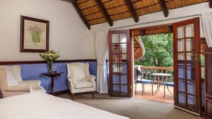 Quarto com uma cama, duas cadeiras, uma mesa pequena com um vaso de flores e uma janela grande com vista para o verde.