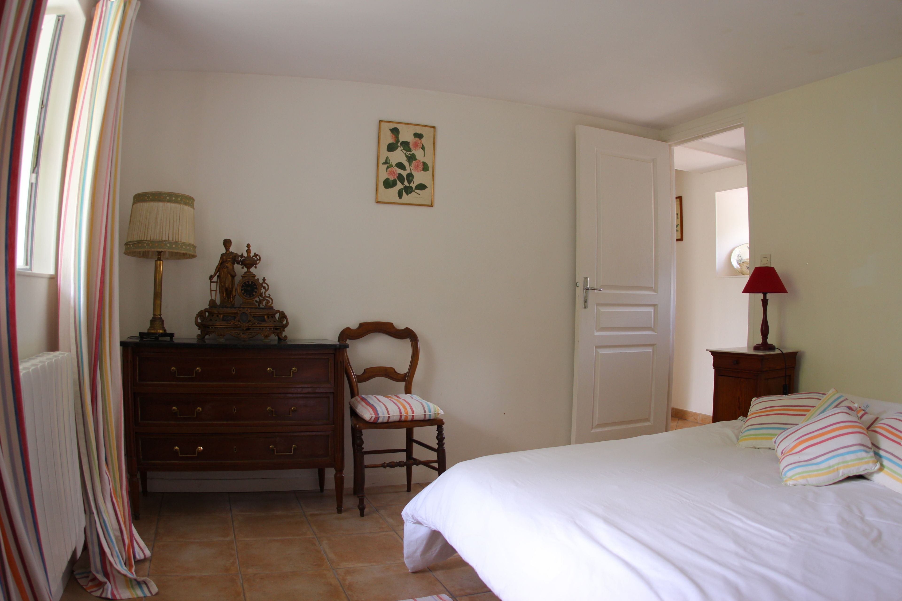 Um quarto com cama, cômoda, cadeira, abajur e porta.