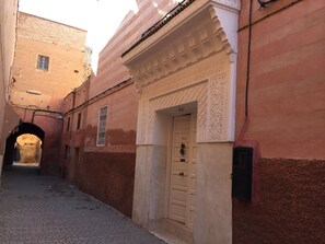 Uma rua estreita com arquitetura tradicional, incluindo uma porta com esculturas detalhadas e uma janela com treliça.