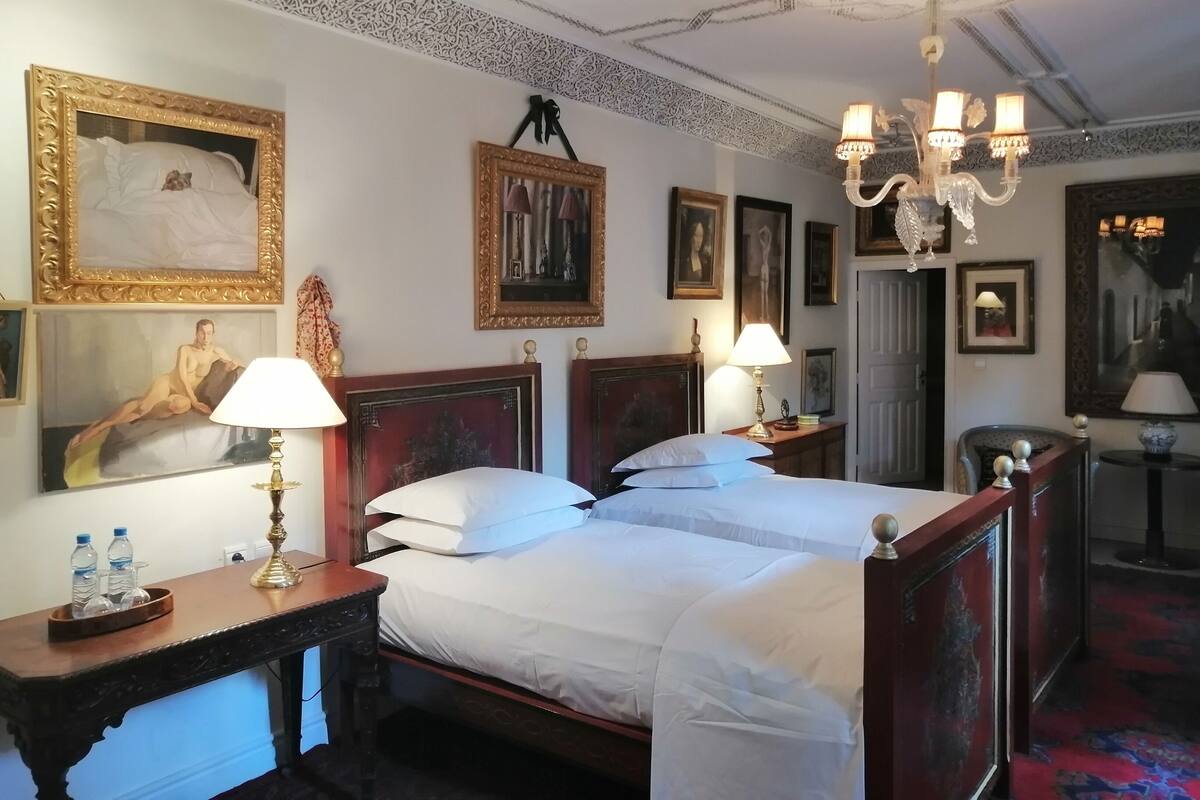 Quarto de hotel com duas camas, teto decorado e várias obras de arte emolduradas.
