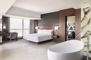 Quarto de hotel moderno com uma cama grande, área de estar, banheira e vista para a cidade.