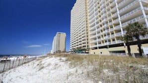 Um hotel alto com várias varandas, uma praia de areia e um céu azul límpido.