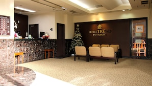 Uma área de recepção de hotel com uma árvore de Natal, um balcão de recepção e um espaço de estar com cadeiras.