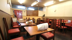 Um restaurante com mesas de madeira e cadeiras estofadas vermelhas, uma grande janela com persianas e uma cortina vermelha.