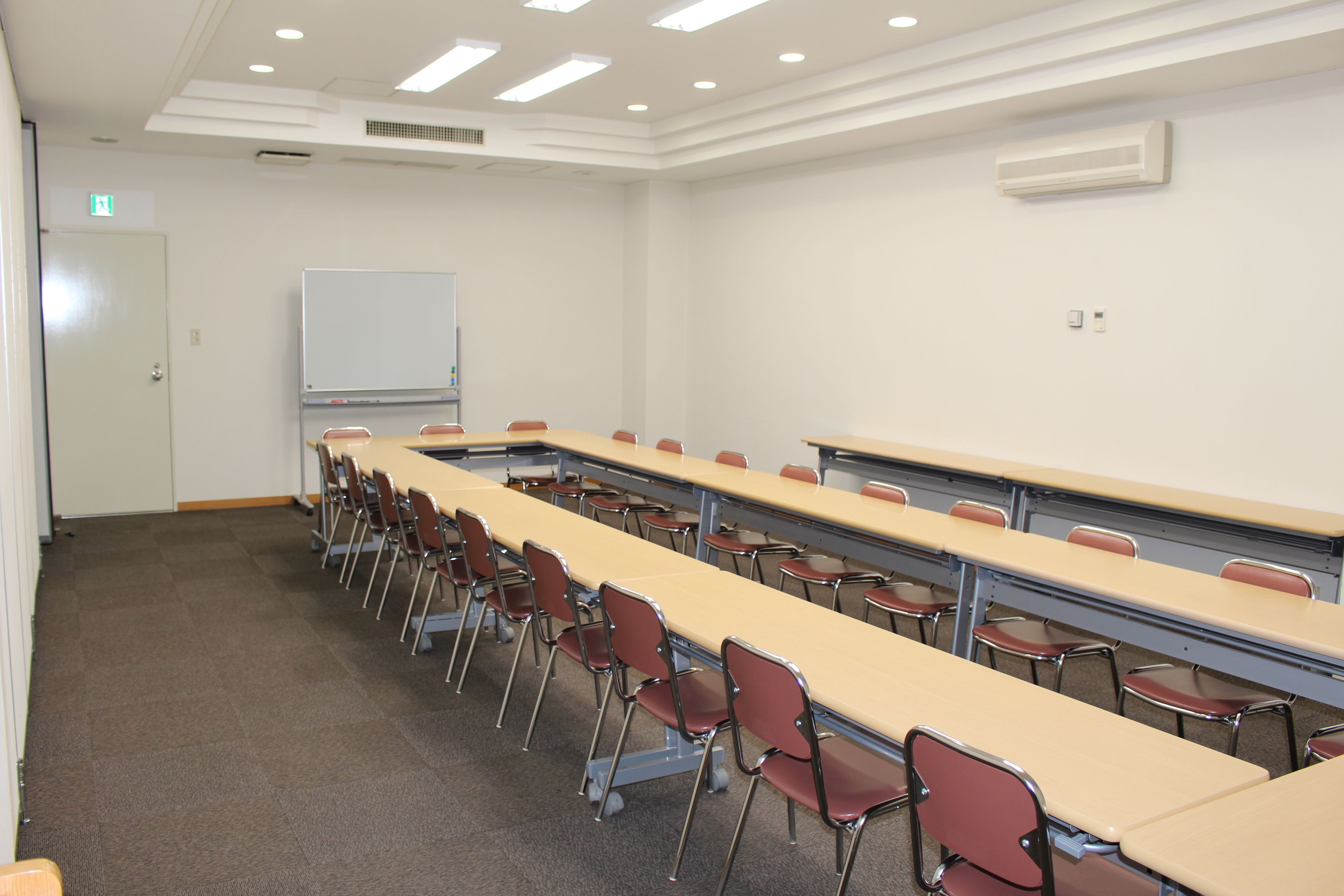 Uma sala de conferências com mesas e cadeiras compridas, um quadro branco e um sinal de saída.