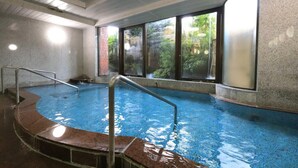 Piscina interior com paredes de vidro transparente, escada de metal e chão revestido de azulejos.