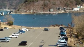Um parque de estacionamento com carros, uma ponte e montanhas ao fundo.