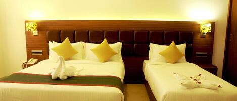 Quarto de hotel com duas camas, cada uma com roupa de cama branca e almofadas amarelas. Possui cabeceira de madeira, telefone ao lado da cama e luminária fixada na parede.