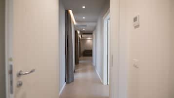 Um corredor com uma porta à esquerda, um luminário no teto e um termostato na parede.
