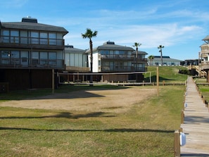 Um imóvel à beira-mar com deck de madeira, quadra de voleibol e edifícios com vários andares e varandas.