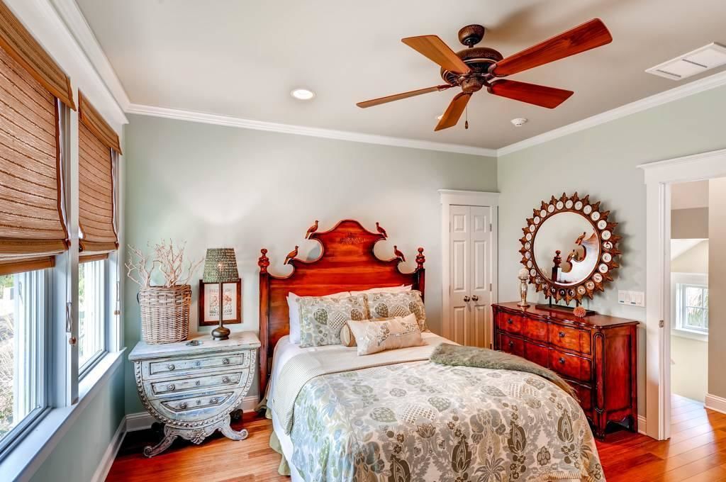 Quarto com cama de madeira, ventoinha no teto, penteadeira, espelho e janela com persianas.
