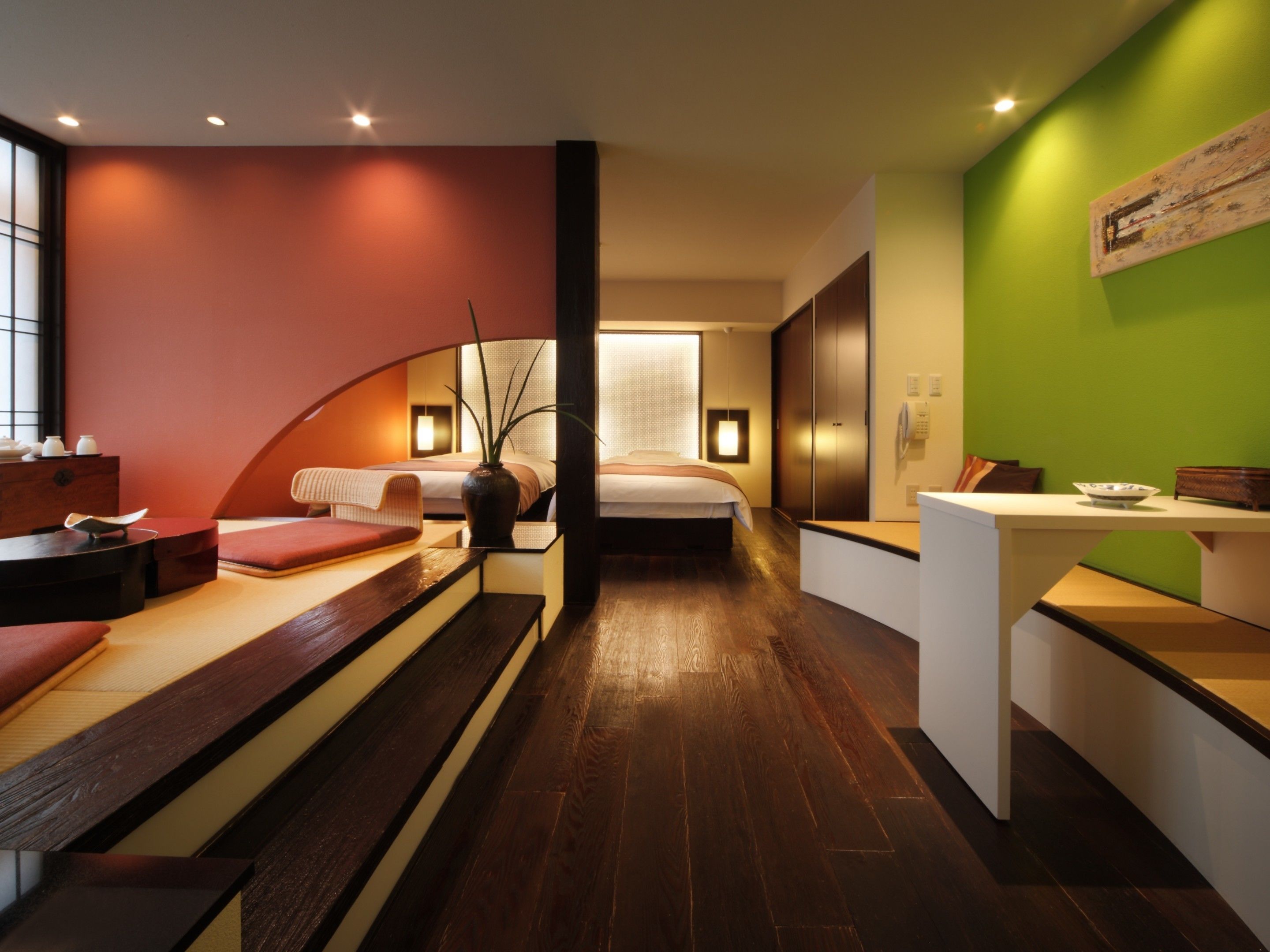 Quarto de hotel moderno com área de estar curvada, uma cama, uma mesa de trabalho e uma parede verde de destaque.