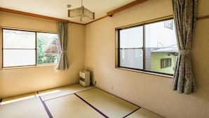 Quarto com piso de esteira de tatame, ventilador de teto e grandes janelas com cortinas.