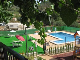Piscina com deck cercado, cadeiras de descanso e guarda-sol vermelho.