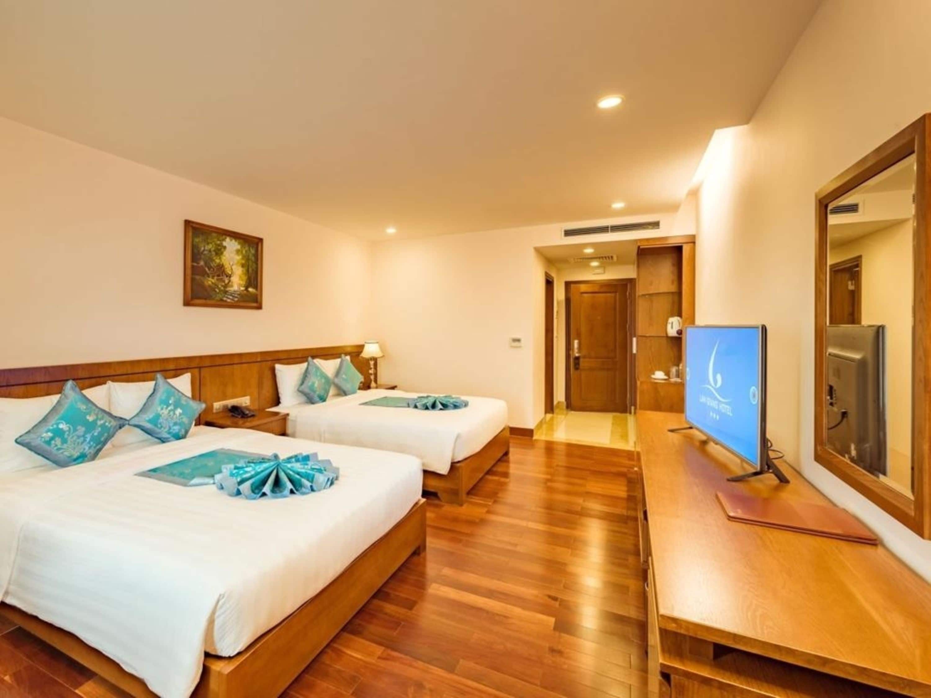 Quarto de hotel com duas camas, uma televisão e uma escrivaninha de madeira.