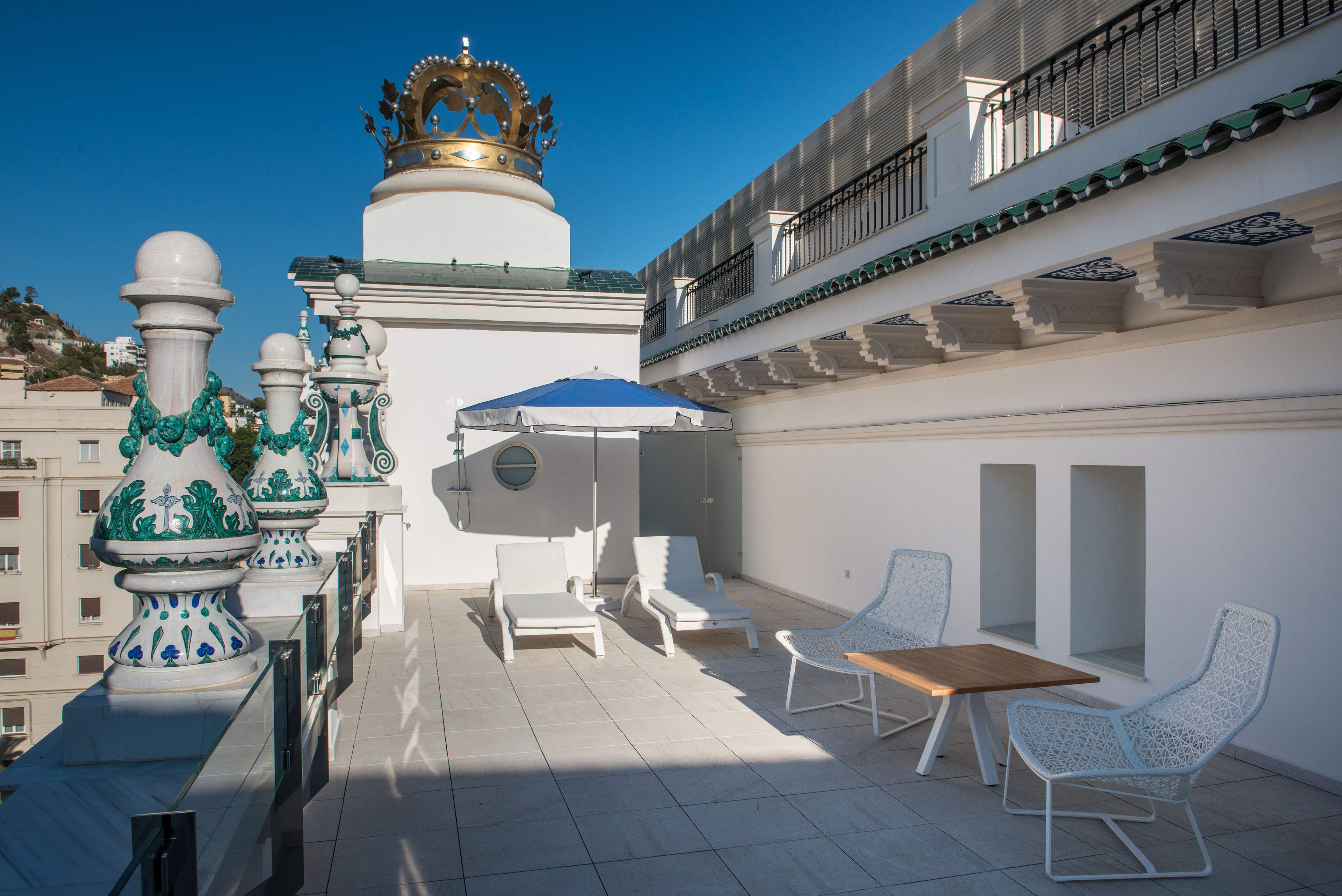 Um terraço no telhado com cadeiras de descanso brancas, uma mesa de madeira e vasos decorativos brancos e verdes.
