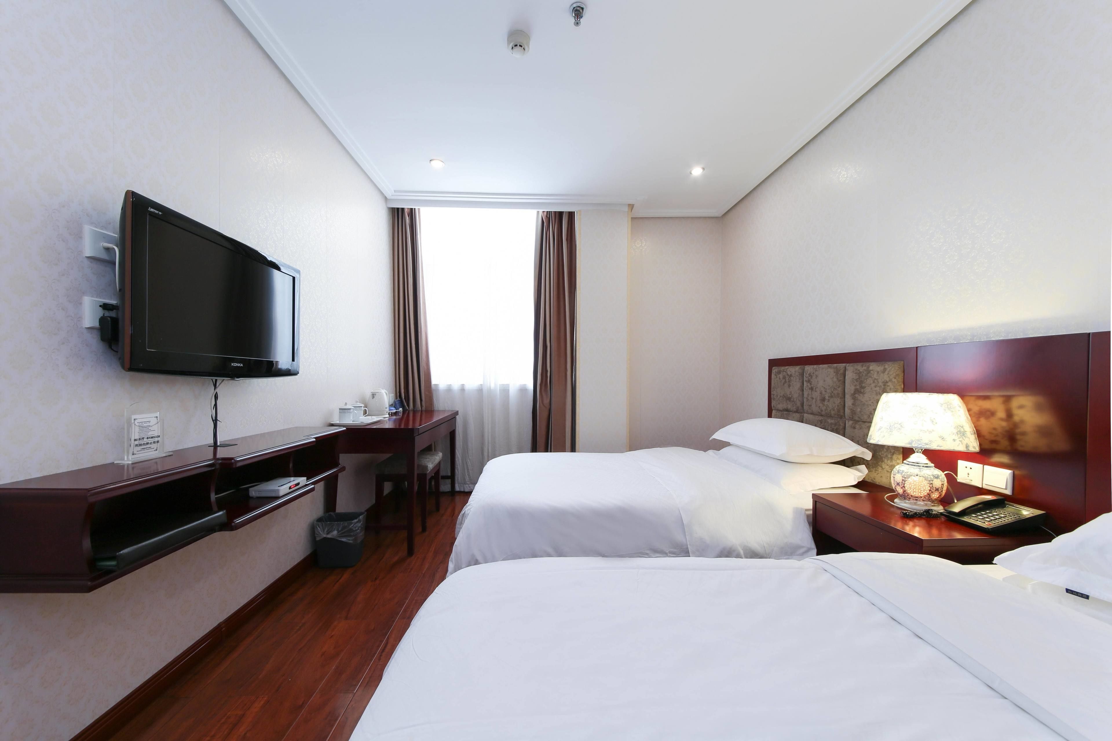 Quarto de hotel com duas camas, uma escrivaninha com televisão, candeeiro e telefone.