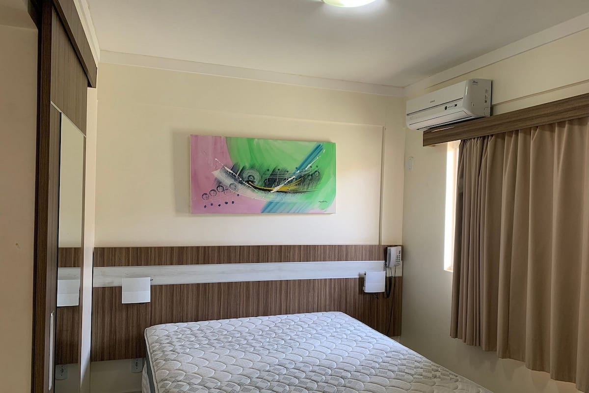 Quarto de hotel com cama, ar condicionado na parede, um quadro e telefone.