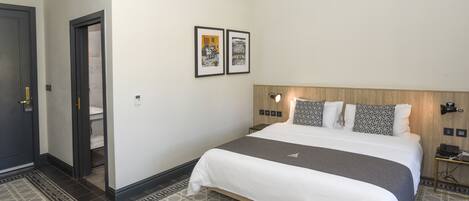 Quarto de hotel com cama, porta e duas imagens emolduradas na parede.