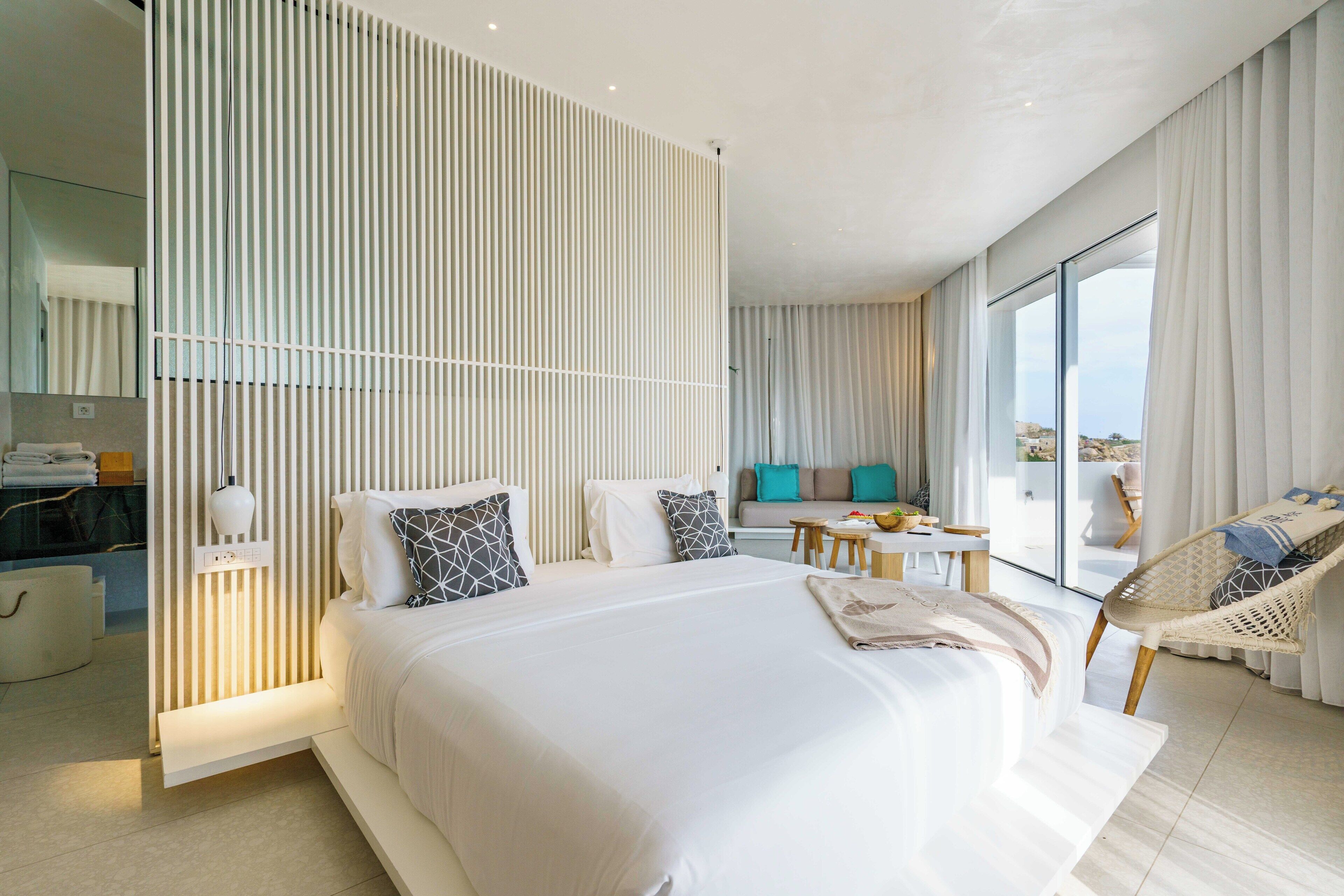 Quarto de hotel moderno com uma cama grande, área de estar com uma mesa e vista para a cidade.