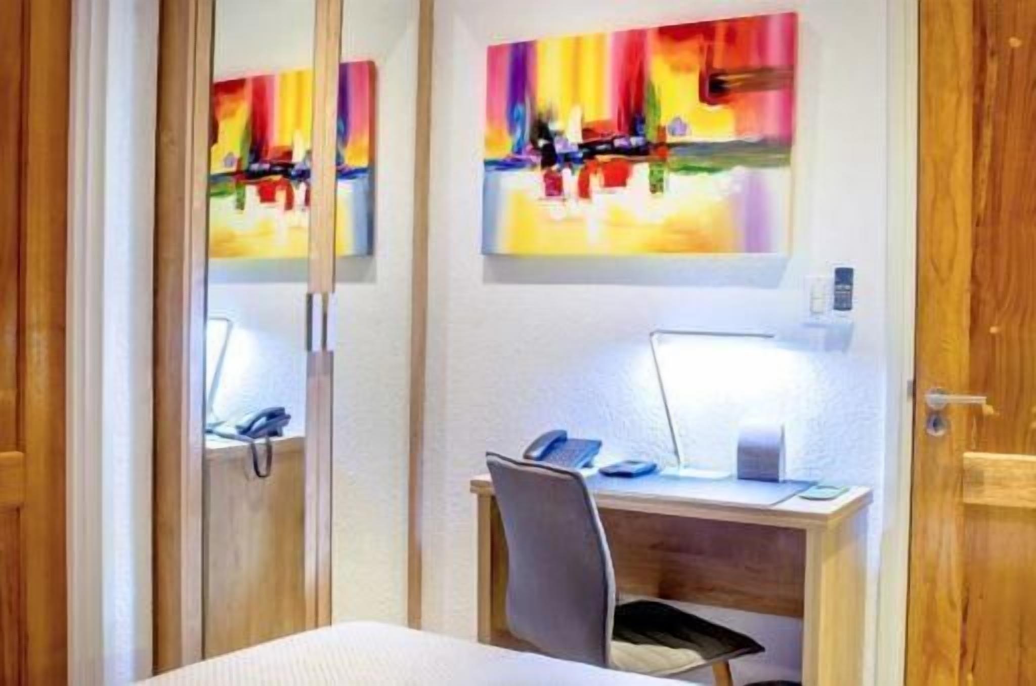Quarto de hotel com escrivaninha, cadeira e duas pinturas na parede.