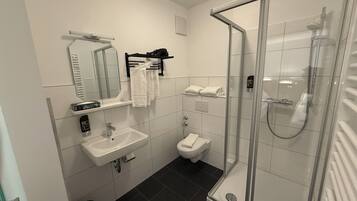 Uma casa de banho moderna com cabine de duche em vidro, lavatório branco, sanita e espelho.