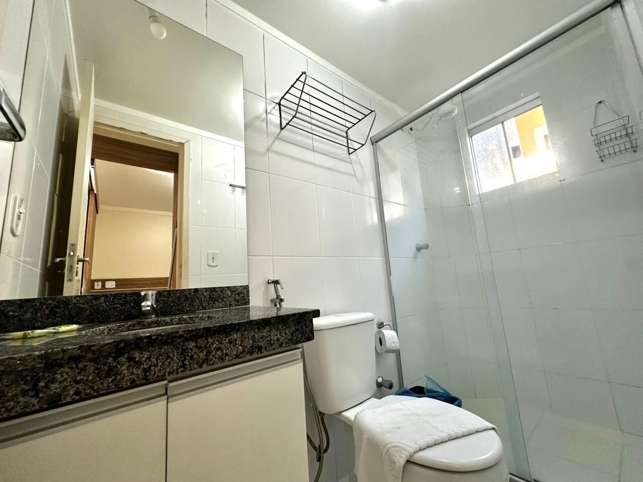 Casa de banho com chuveiro, sanita e lavatório com bancada.