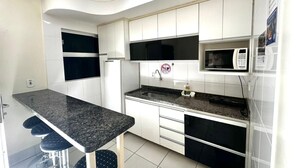 Uma cozinha compacta com bancada de granito, armários brancos, micro-ondas e pia.