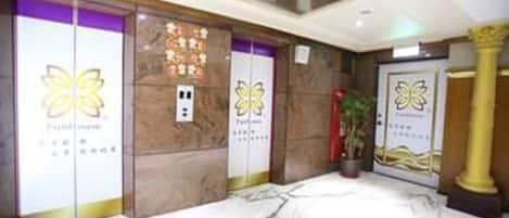 Um hall de hotel com piso de mármore, uma mesa de recepção e uma parede com o logotipo floral.