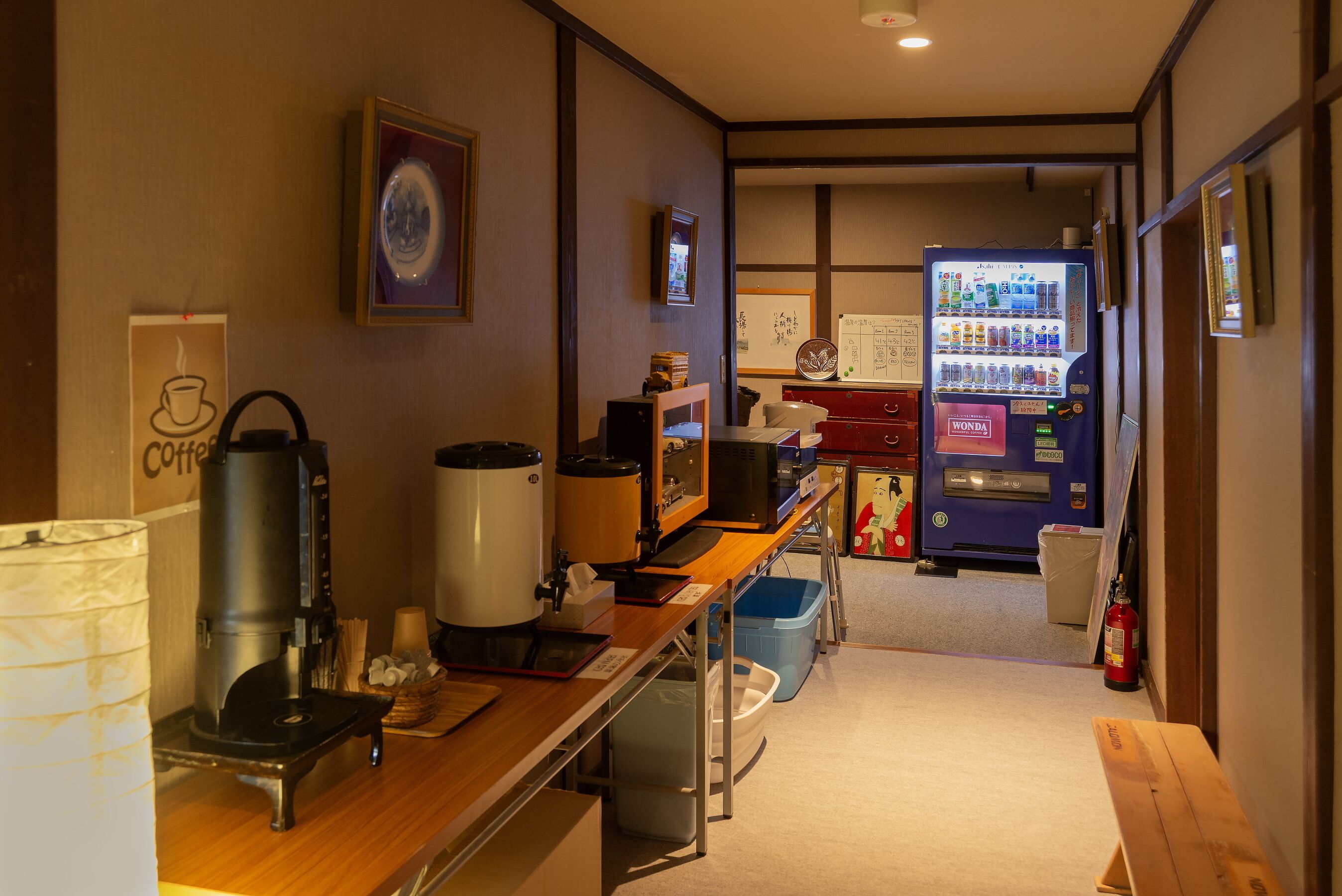 Um pequeno café com uma máquina de café, uma máquina de vendas e um balcão de madeira.