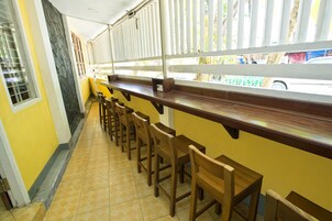 Um restaurante com paredes amarelas, banquetas de madeira e vista para a rua através de grandes janelas.