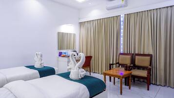 Quarto de hotel com duas camas, uma mesa de madeira, duas cadeiras, uma escrivaninha e uma janela com cortinas.