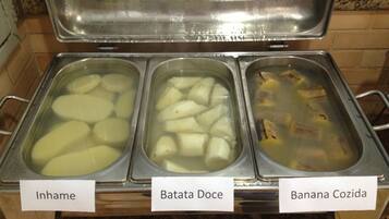 Buffet com recipientes identificados de inhame, batata doce e banana cozida.