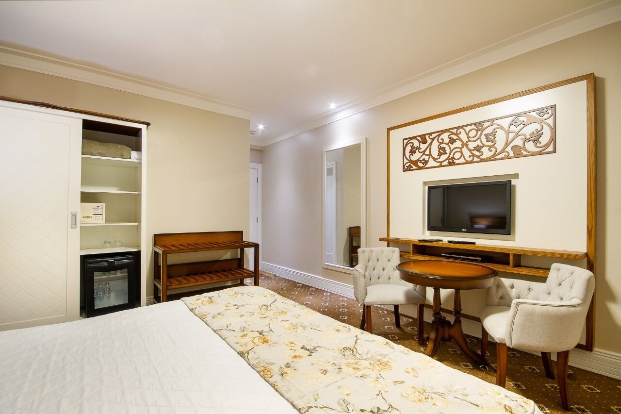 Quarto de hotel com uma cama, uma escrivaninha com cadeira, televisão e guarda-roupa.