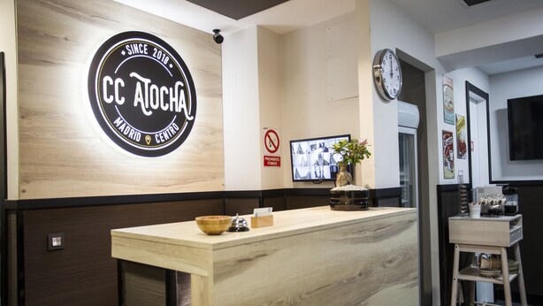 Uma área de recepção com balcão de madeira, um relógio, uma televisão e um aviso proibindo fumar.