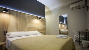 Quarto de hotel moderno com uma cama grande, luminárias de cabeceira, um espelho, uma mesa pequena e uma cadeira.
