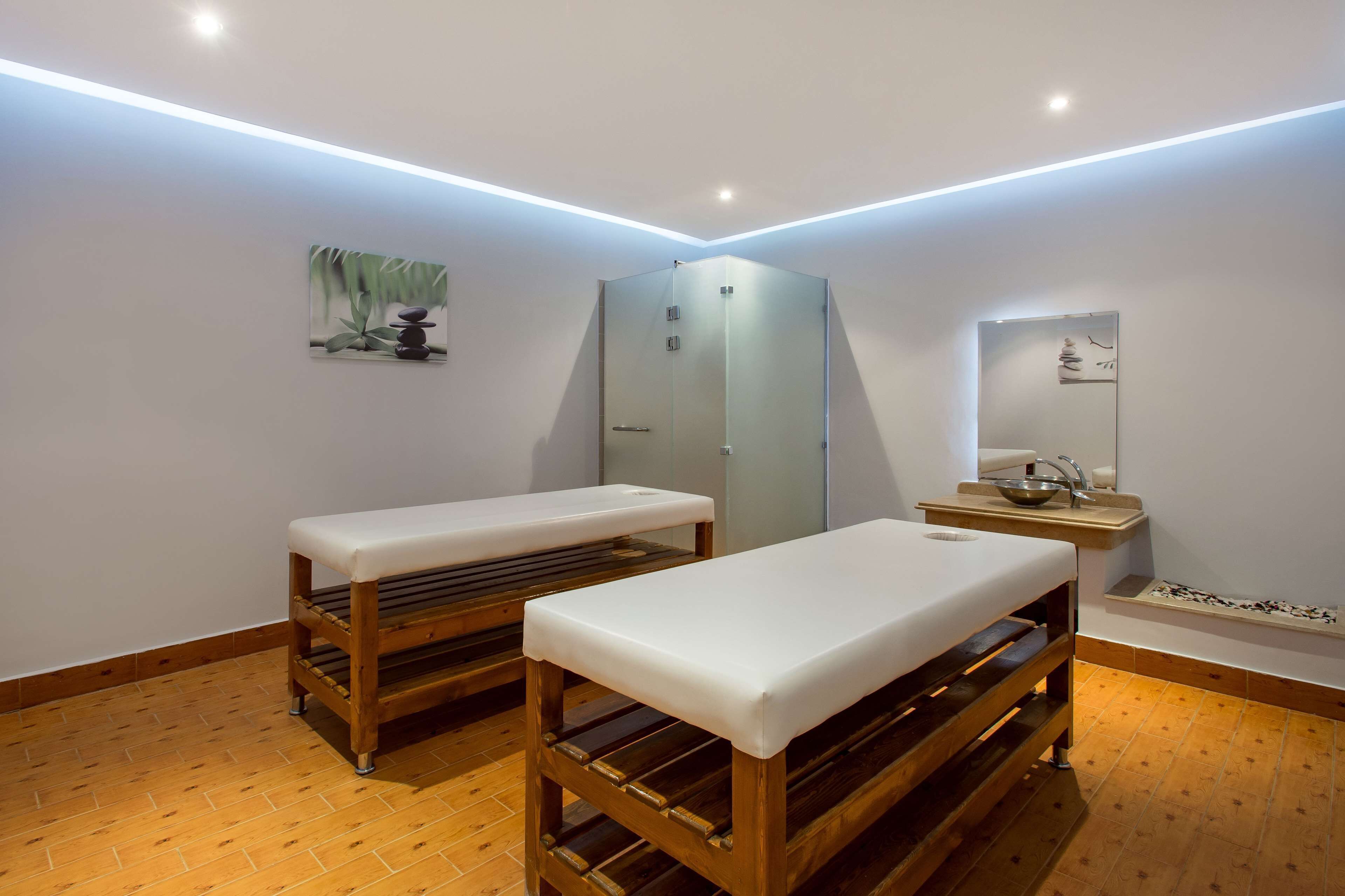Um spa moderno com duas mesas de massagem de madeira, um box de chuveiro de vidro, uma pia pequena e um espelho fixado na parede.