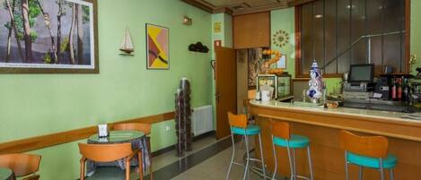 Interior de restaurante com área de bar, paredes verdes e uma pintura de árvores.