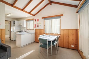 Cozinha compacta com ilha central, vigas de madeira, área de refeições com mesa e cadeiras, e vista para o exterior através de uma janela.