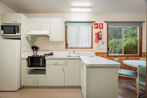 Cozinha compacta com micro-ondas, torradeira e pia. Janela com vista para o verde lá fora.