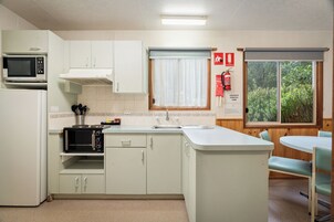 Cozinha compacta com micro-ondas, torradeira e pia. Janela com vista para o verde lá fora.