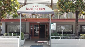Entrada de um hotel chamado 'hotel GLENN', com área de estar coberta ao ar livre e porta de entrada visível.